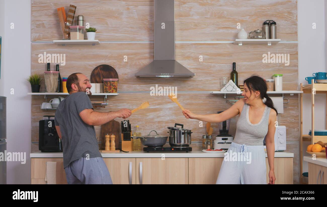 Couple having fun in the kitchen fencing with big spoons during ...