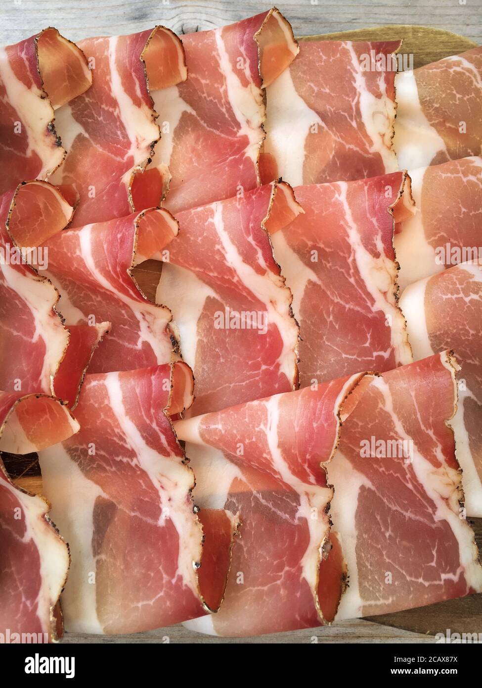Thin slices of delicious South Tyrolean bacon served on a wooden board ...