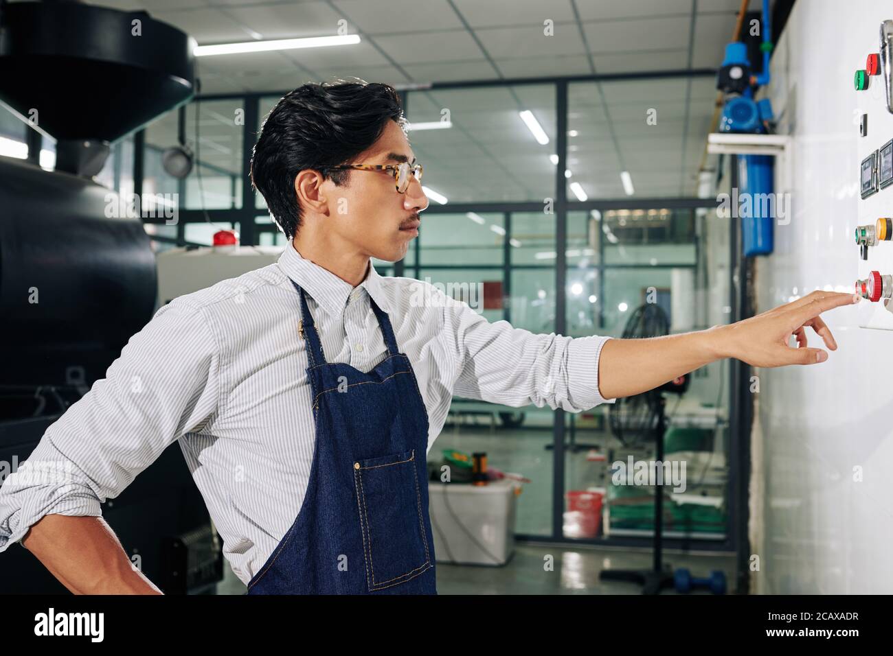 Serious mixed-race coffee roastery worker pushing button on control ...