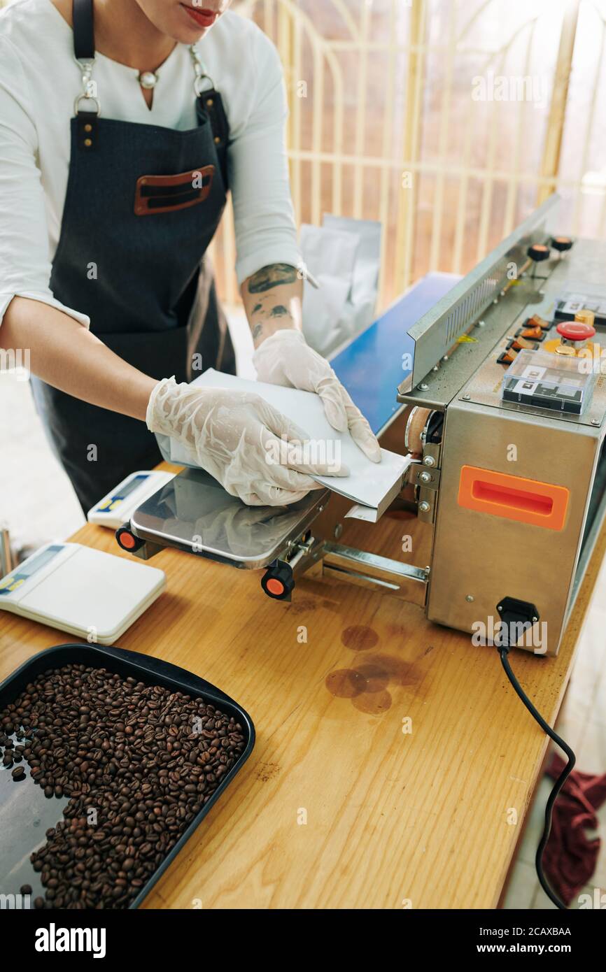 Female roastery worker in apron and rubber gloves sealing seams of ...