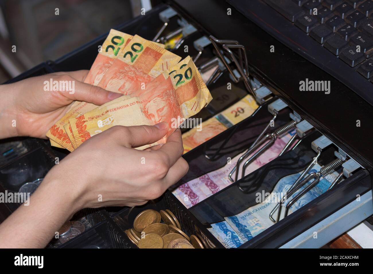 Saleswoman hands at cash register with brazilian money notes and coins ...