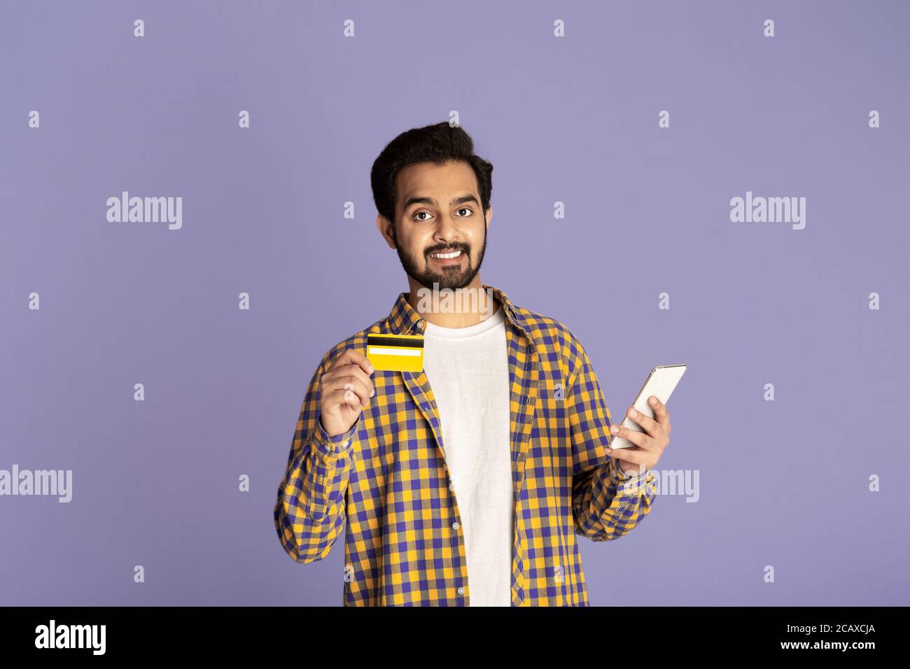 Online shopping. Cheerful Indian man holding mobile phone and credit ...