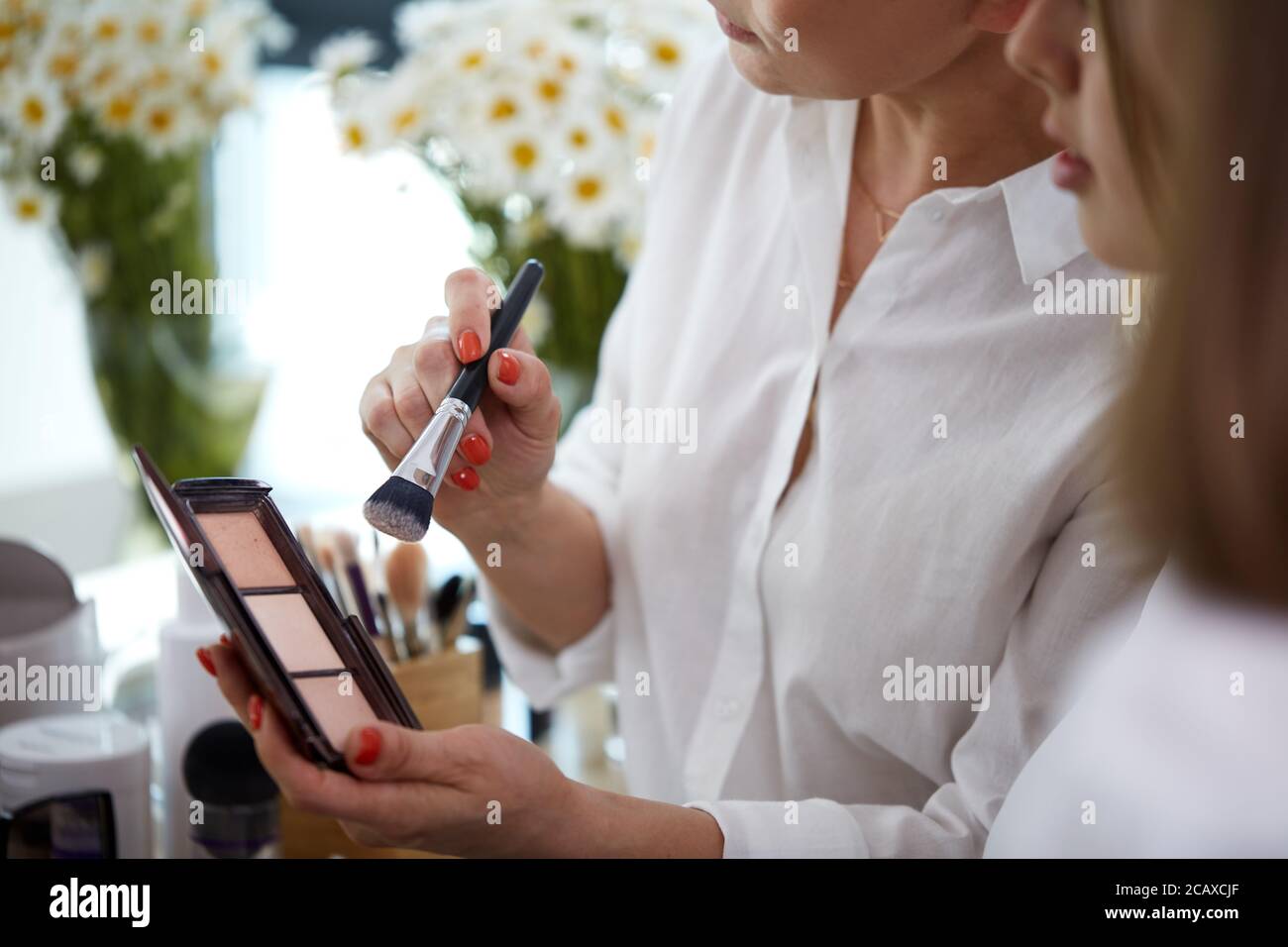 young caucasian make-up artist going to apply blush on model's face ...