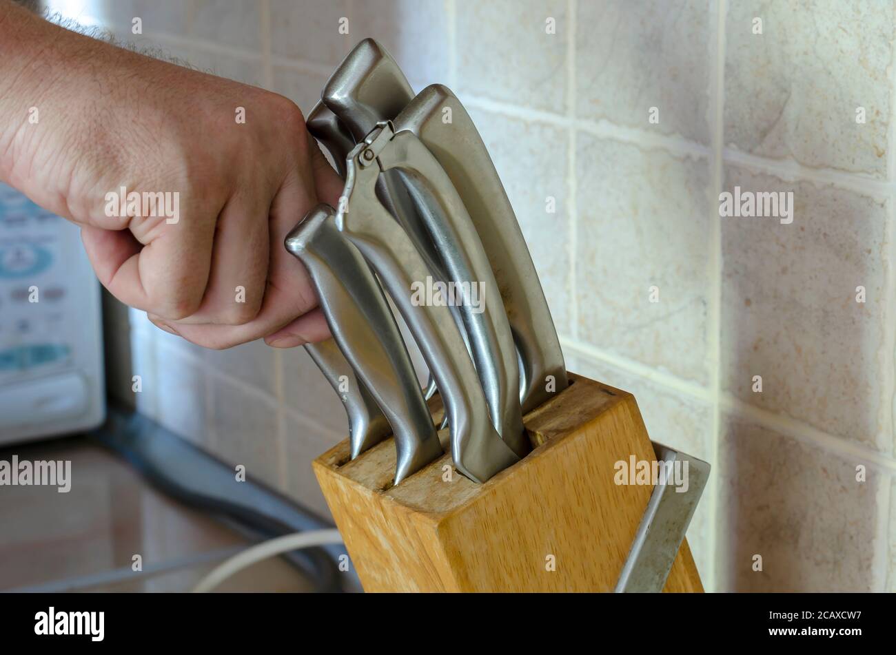 Male hand takes kitchen knife from a wooden stand. Set of metal kitchen ...