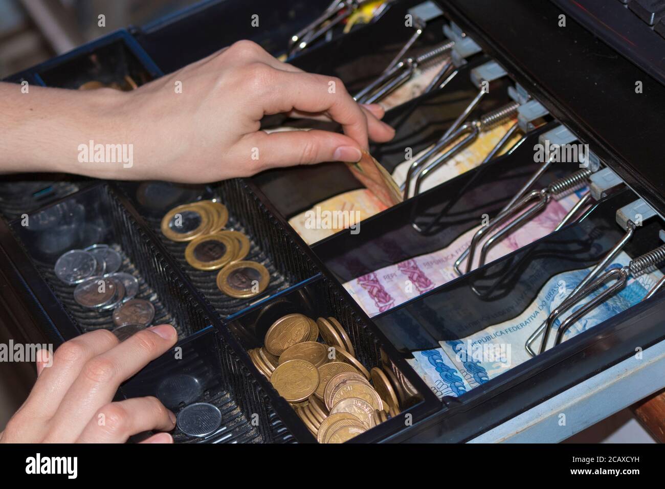 Saleswoman hands at cash register with brazilian money notes and coins ...