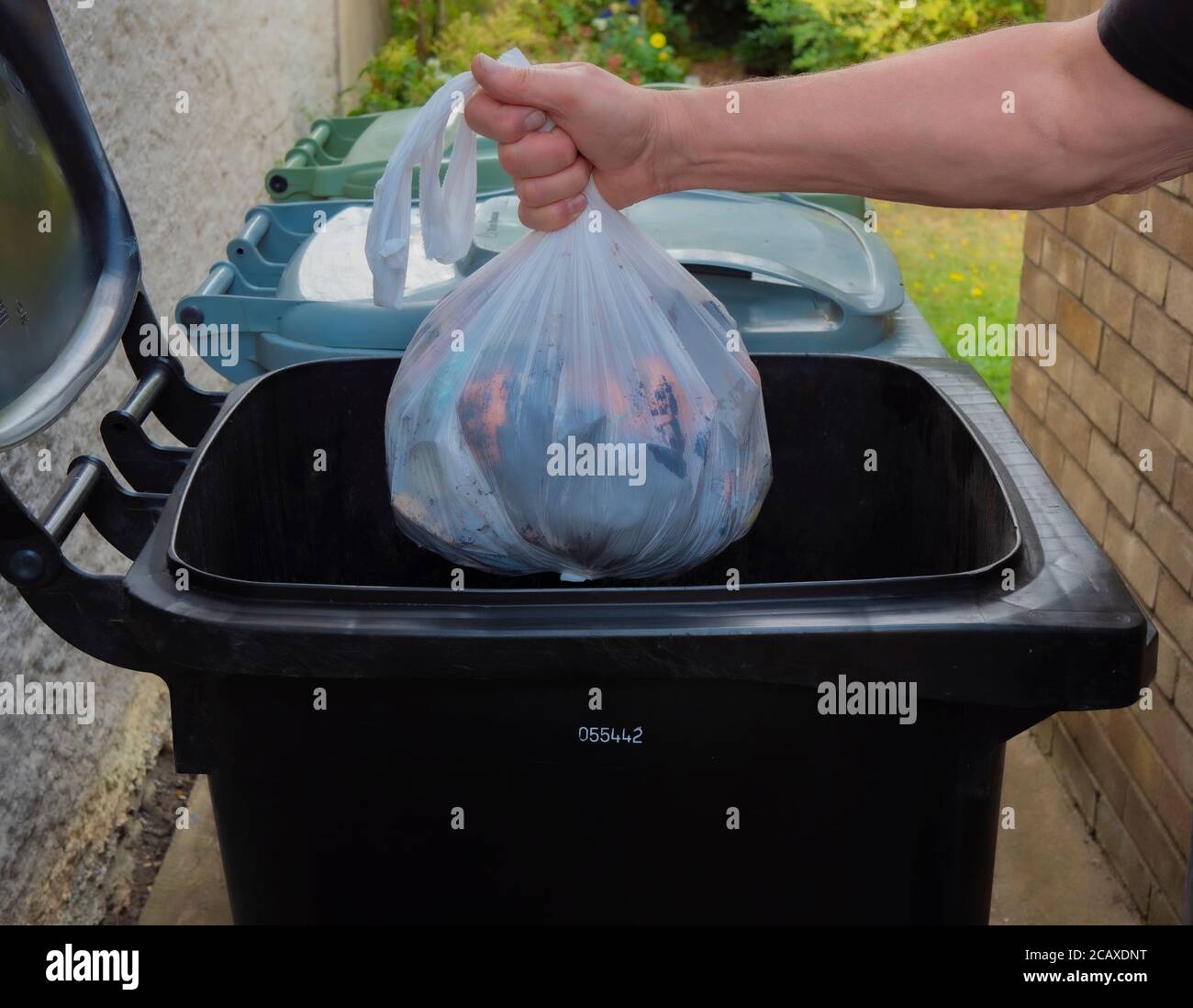 A man’s hand dropping a bag full of food waste into a black non ...
