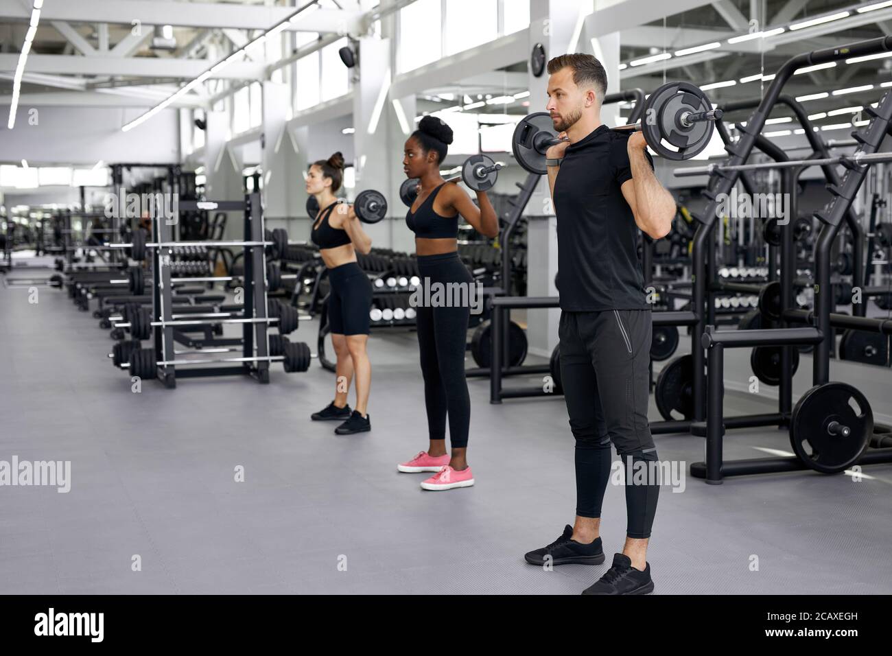 sportive people, multiethnic group perform exercises with heavy weights ...