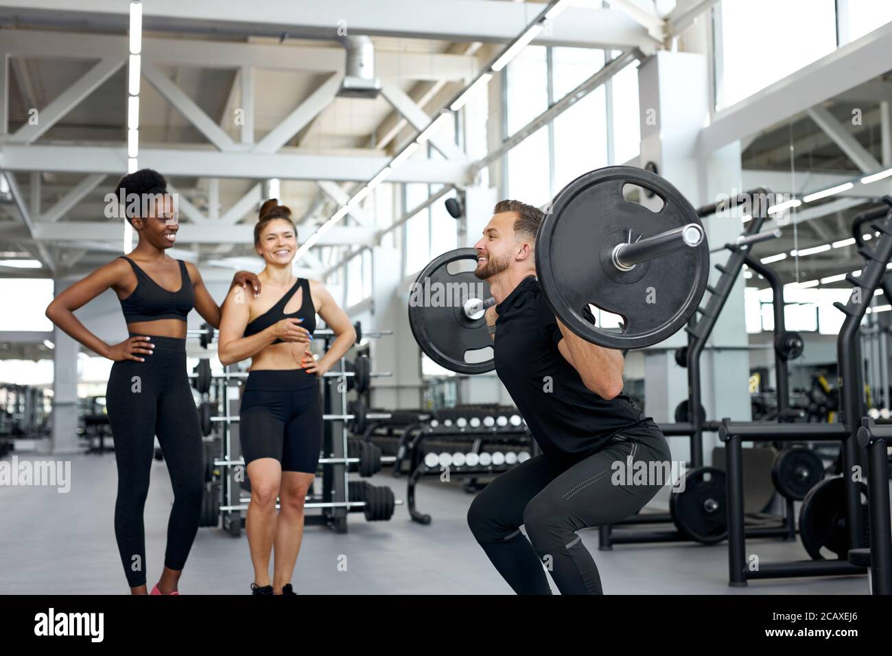 trainer shows exercises with barbell to girls in gym. diverse women ...