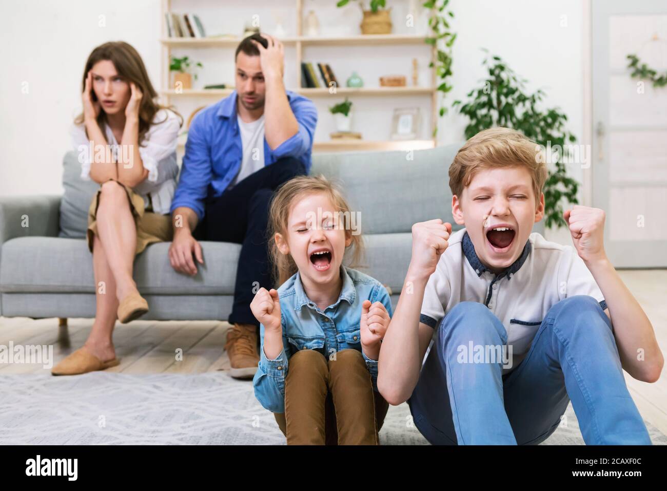 Children Shouting While Parents Covering Ears Sitting On Sofa Indoor ...