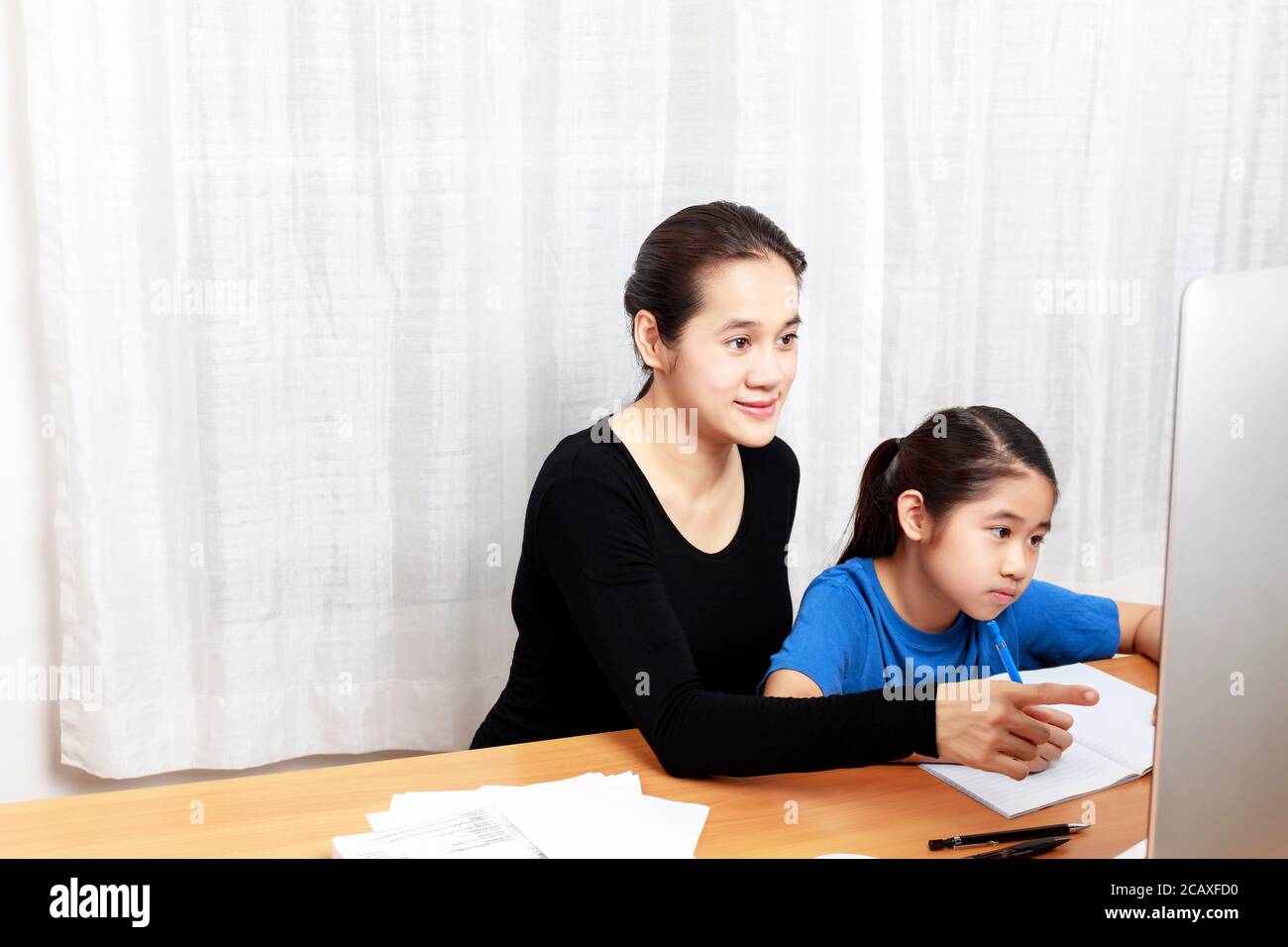 Asian young little girl using pencil to do homework with her mother ...