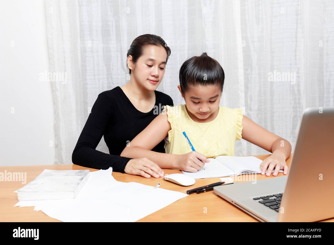 Asian young little girl using pencil to do homework with her mother ...