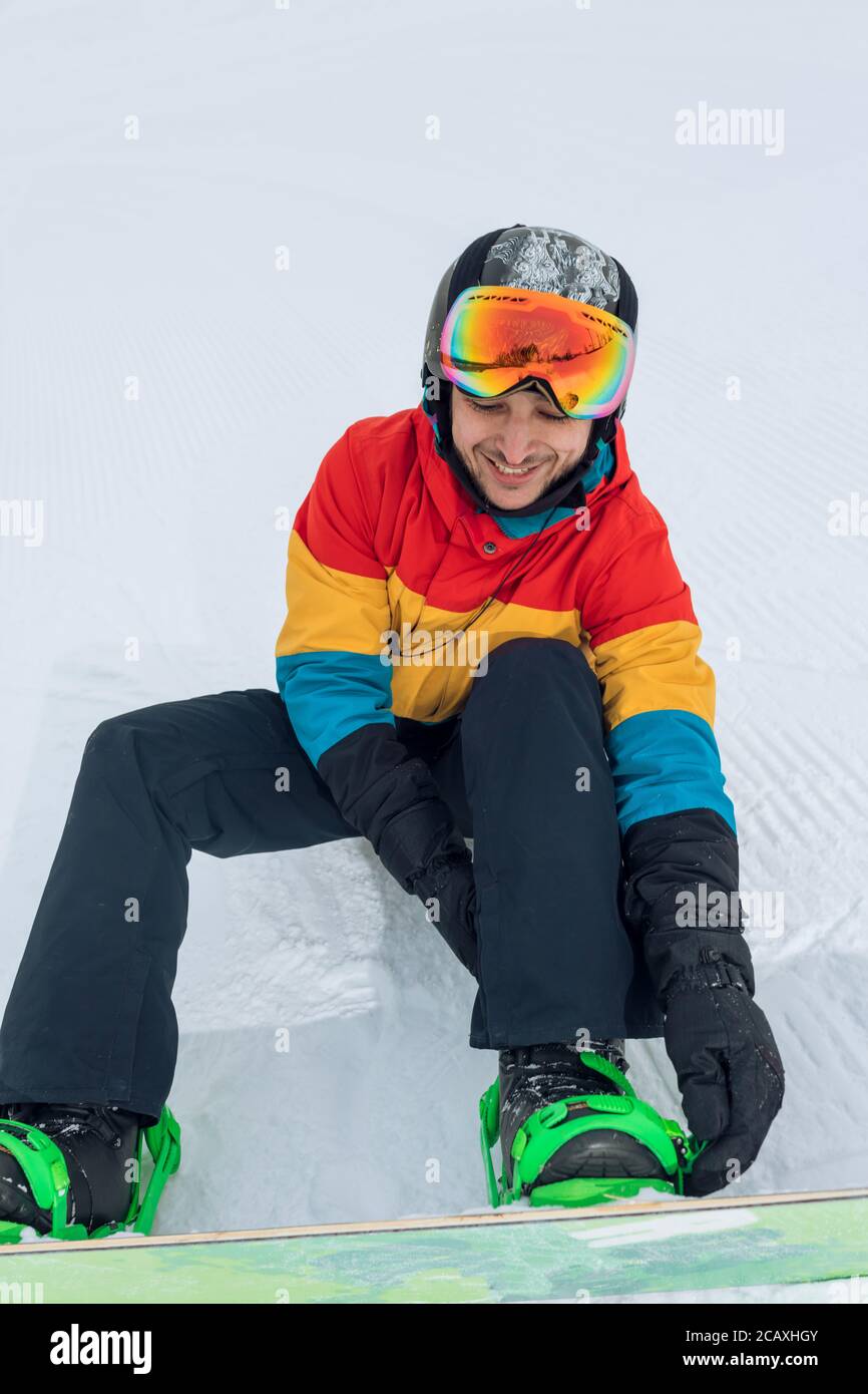good looking guy enjoys putting on boots for snowboarding, full length photo. happiness concept ...