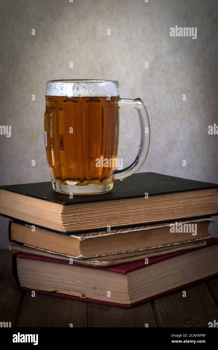 A glass of golden beer over a stack of hardbound books on a wooden ...