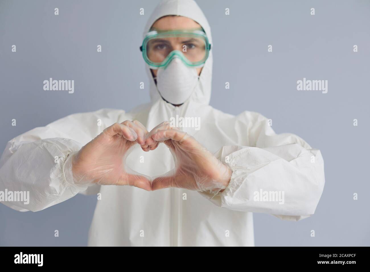 Doctor in hazmat suit showing heart with hands on grey background ...