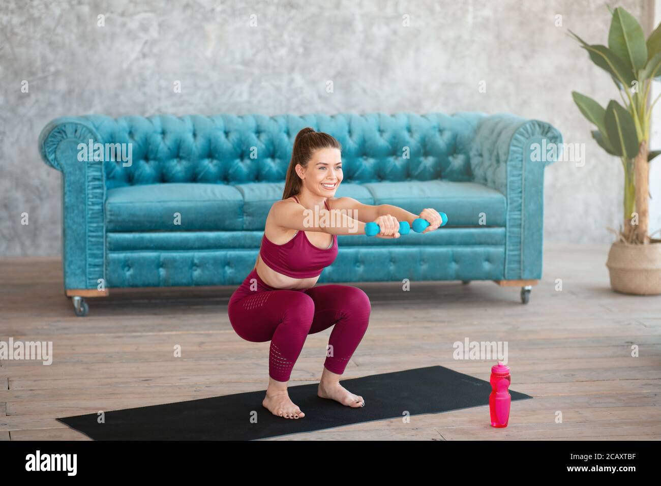 Stay home sports. Attractive fit girl doing squats with dumbbells in ...