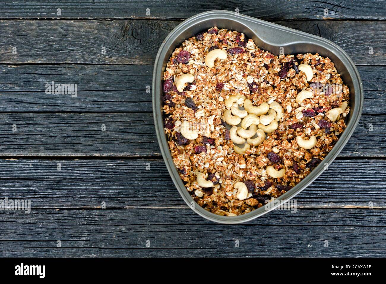 Granola with cashew in a heart-shaped baking dish. Black wooden table ...
