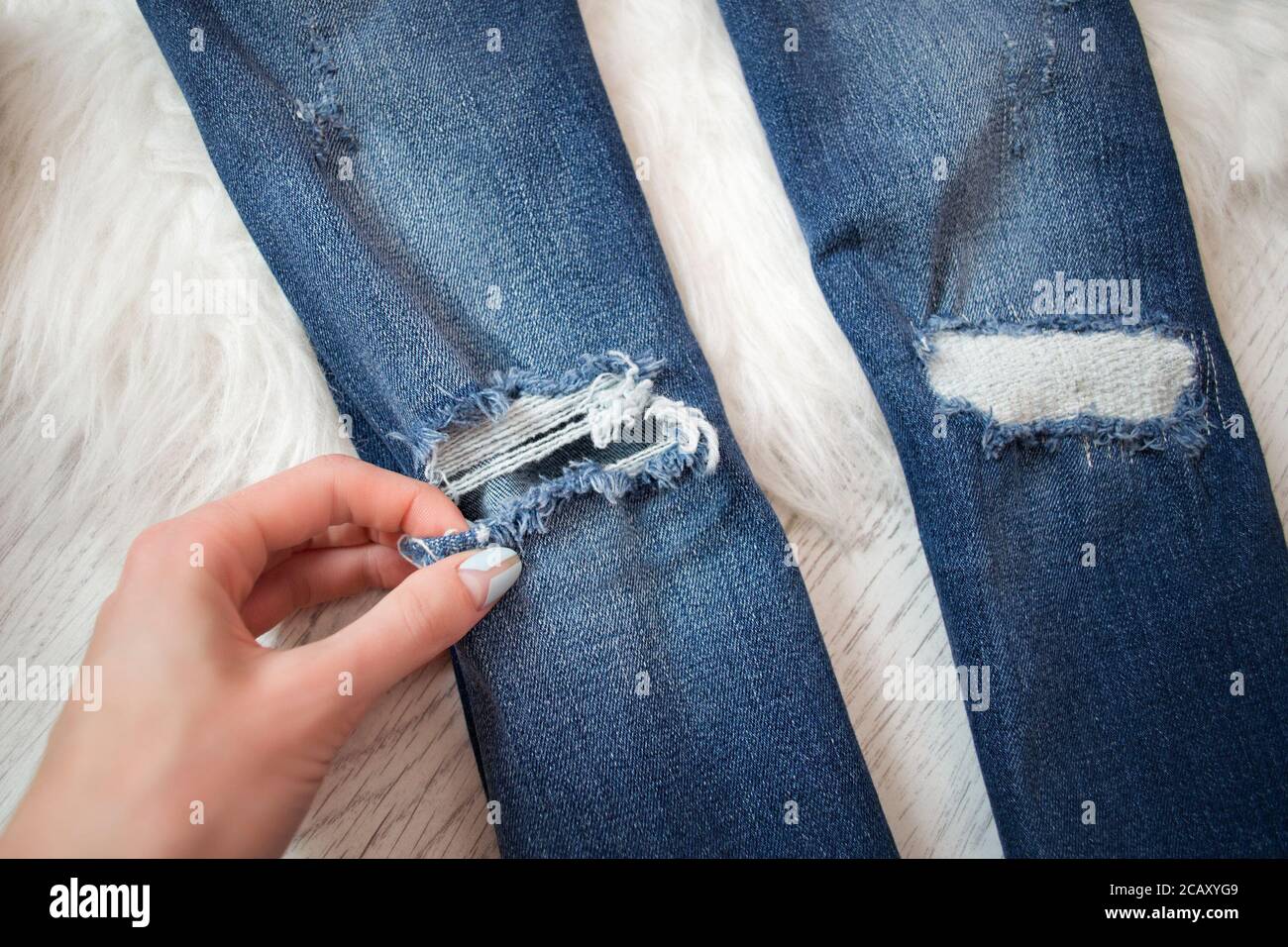 Blue ragged jeans in a female hand. Detail. Fashionable concept Stock ...