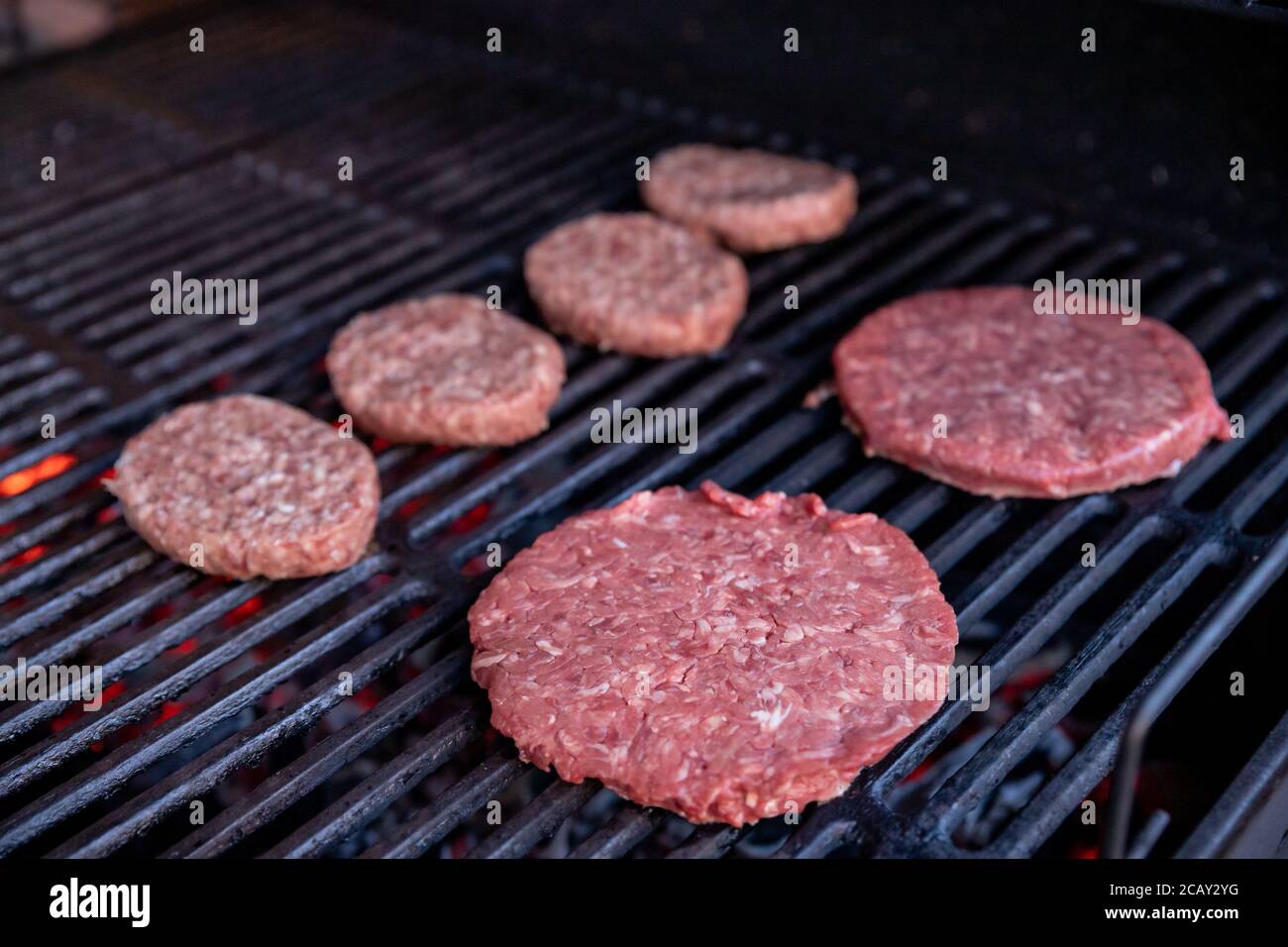 Raw beef burgers with a pinch of salt and black pepper on grill ...