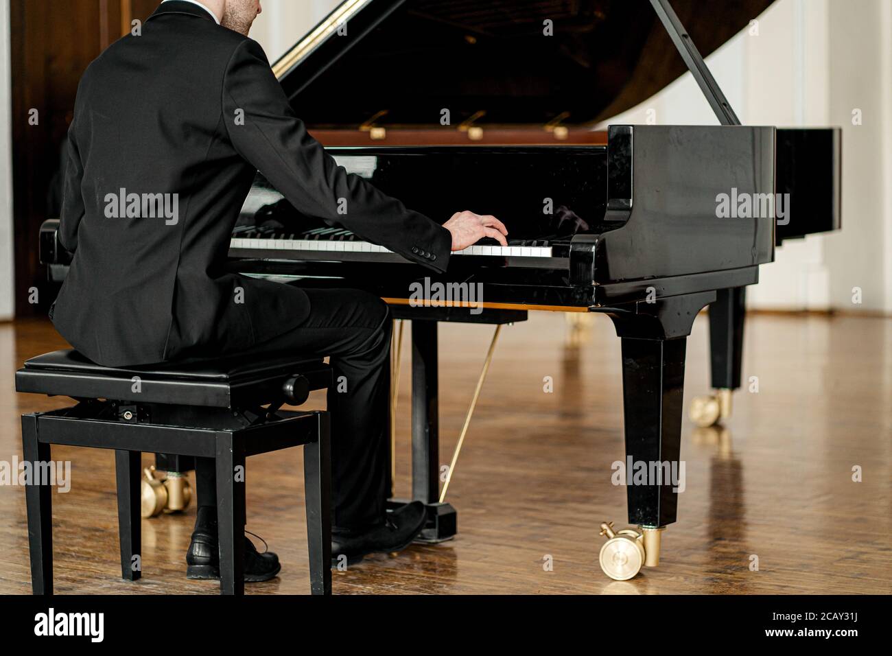 cropped unrecognizable male in suit playing piano on a stage. handsome ...