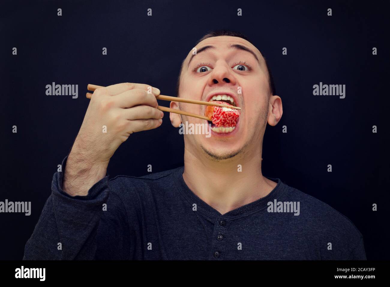 Hungry man eats rolls with chopsticks. Open mouth. Black background ...