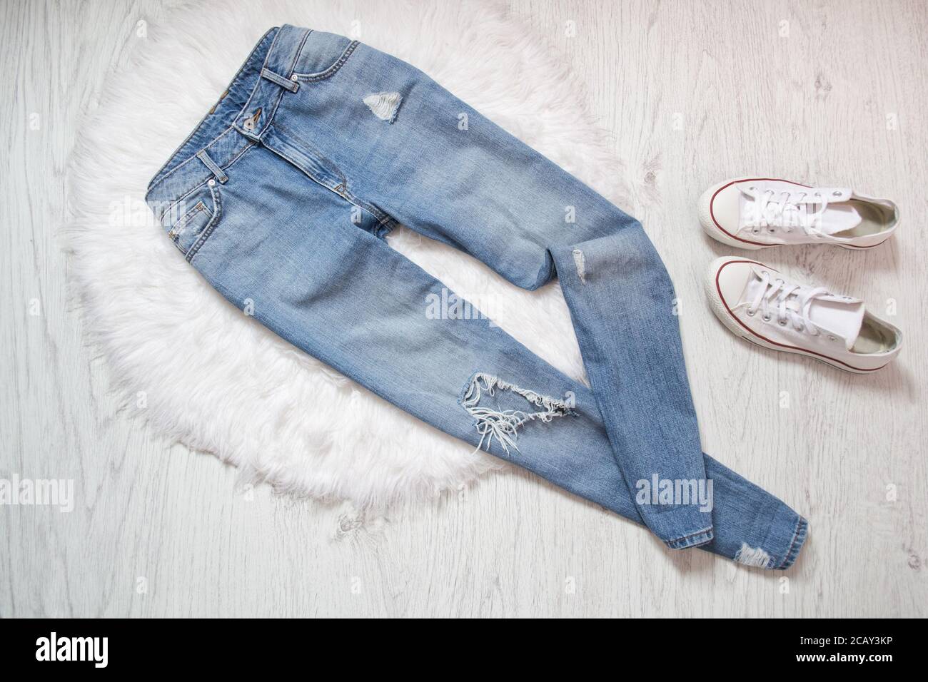 Blue ragged jeans and white sneakers on white fur. Fashionable concept ...