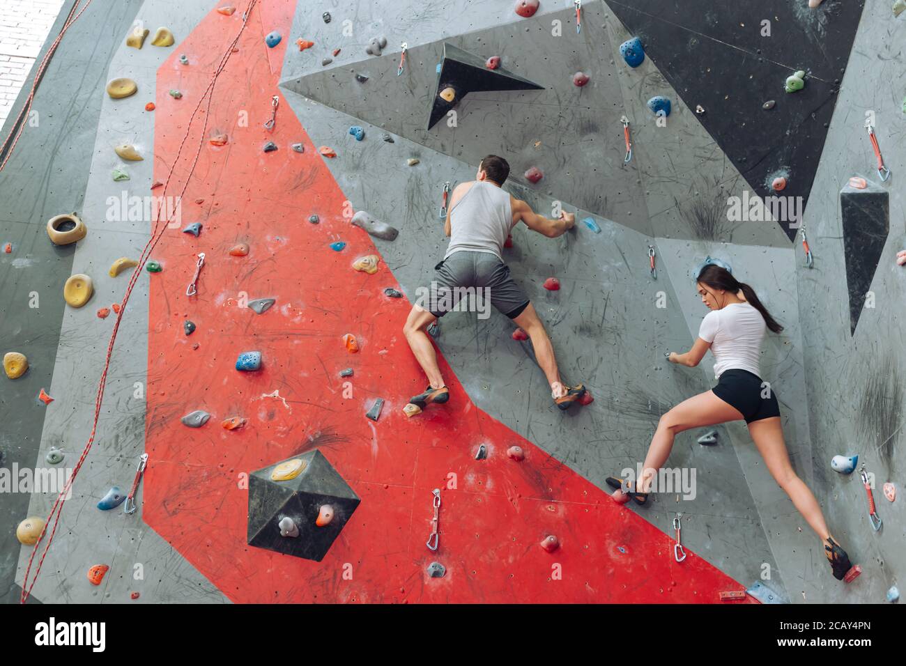 Female climber looking frightened down the climbing wall. Male climber ...