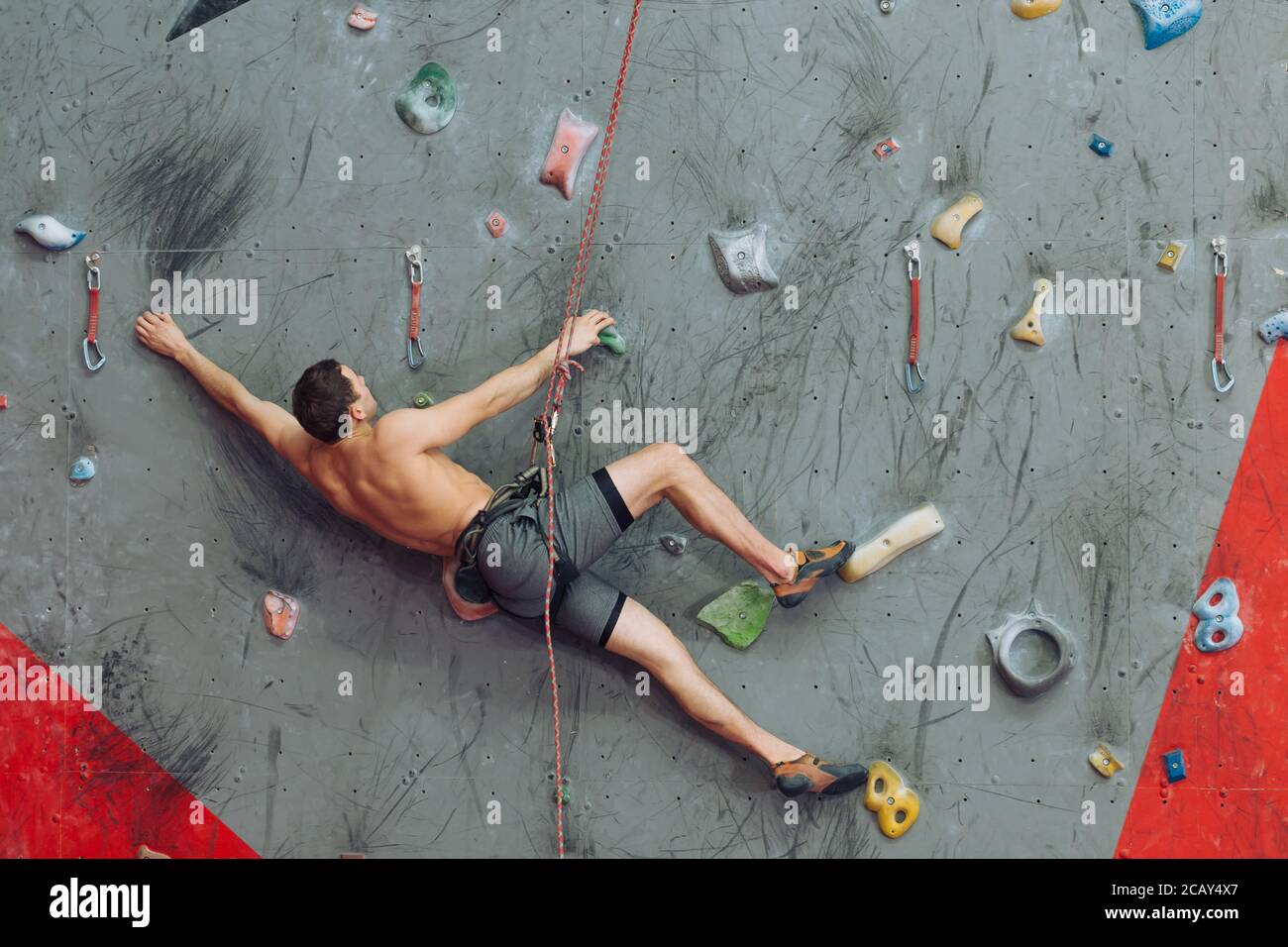 young shirtless man reaching to the rope during bouldering. full length ...