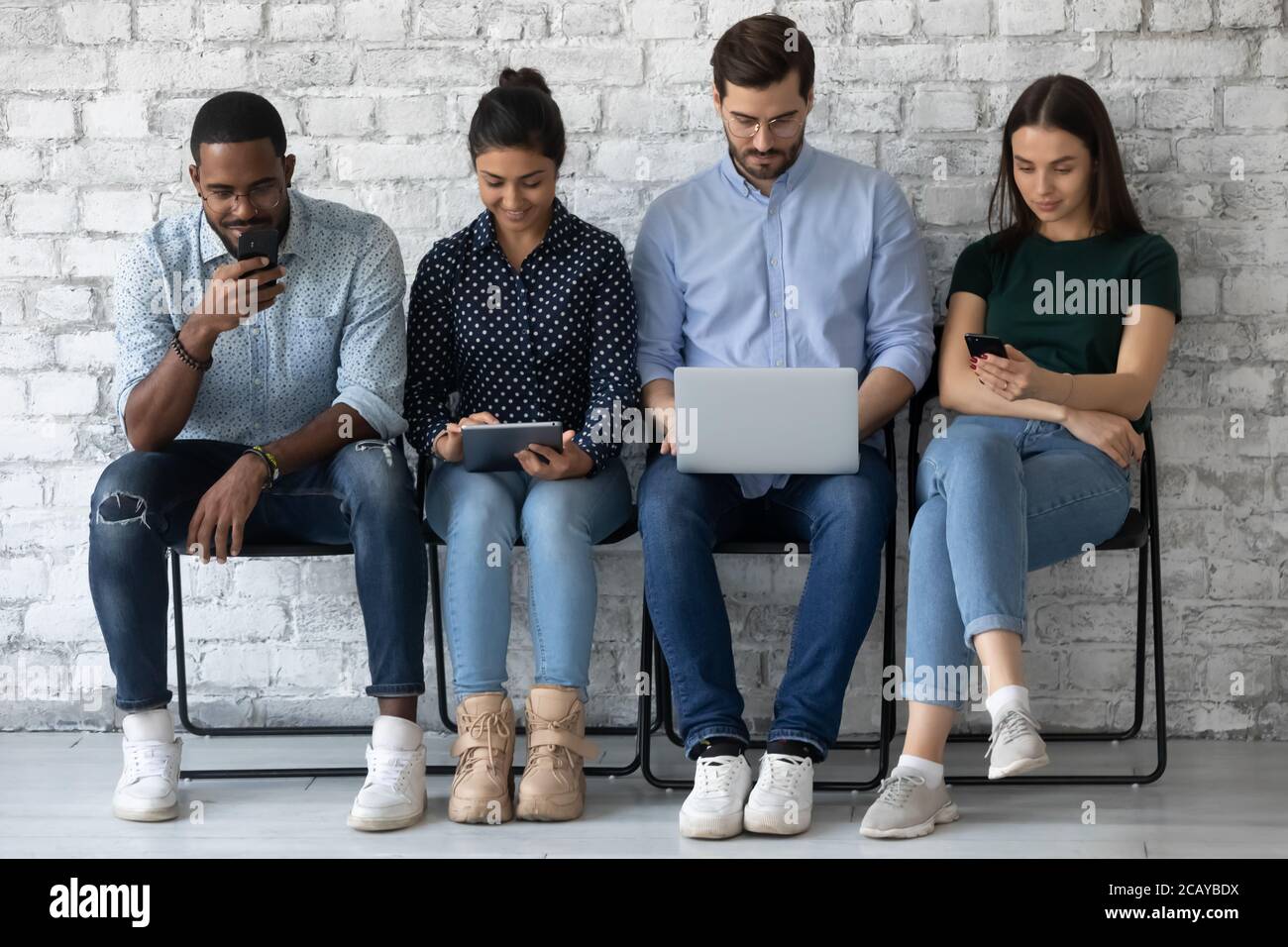 Diverse candidates waiting for job interview, using mobile devices ...
