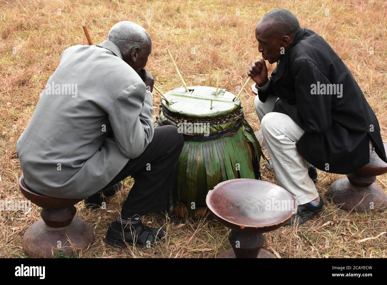 Two Rwandan old men drink from a big pot at a traditional festival ...