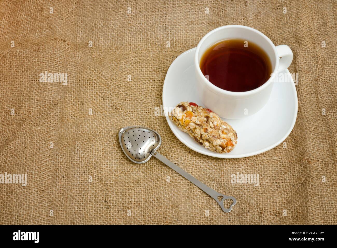 Cup of tea, bar of muesli and tea-strainer on sackcloth. Top view Stock ...