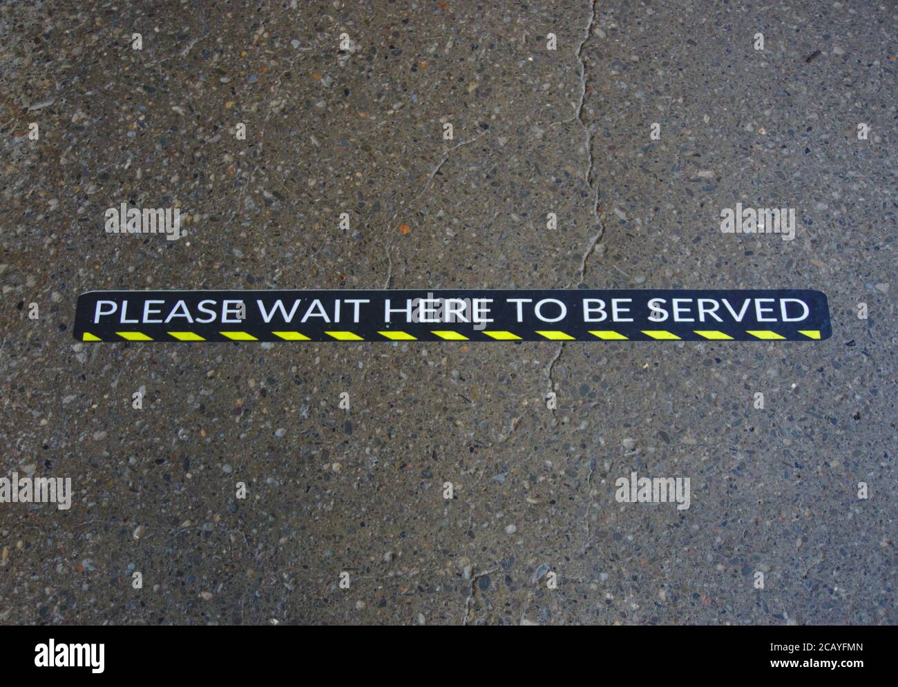 'Please wait here to be served' social distancing sign on the pavement ...