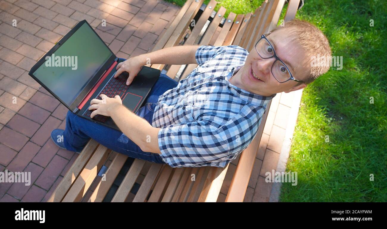 The guy sits on a park bench and works at a laptop. Smiling face Stock ...