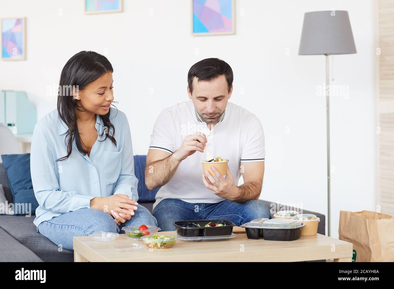 Portrait of smiling man and woman opening food delivery containers ...