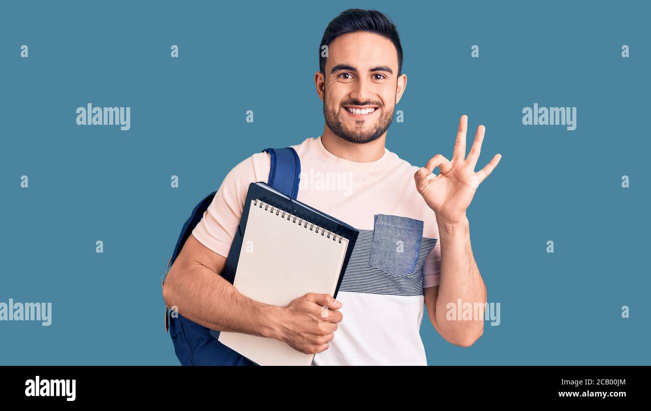 Young handsome man wearing student backpack and notebook doing ok sign ...
