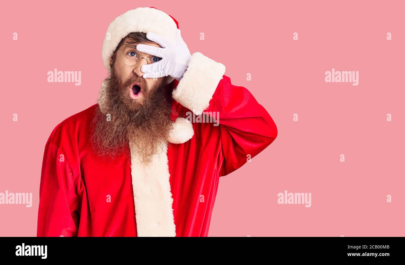 Handsome young red head man with long beard wearing santa claus costume ...
