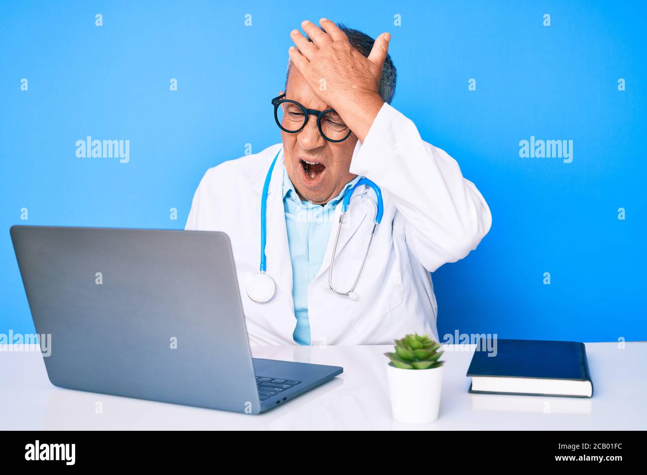 Senior handsome man with gray hair wearing doctor uniform working using ...