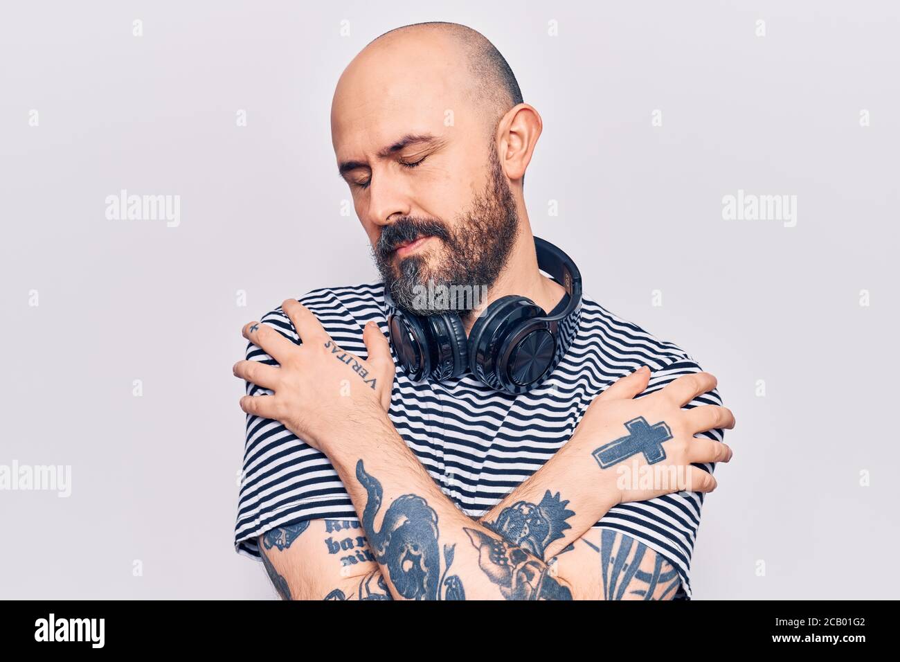 Young handsome man listening to music using headphones hugging oneself ...