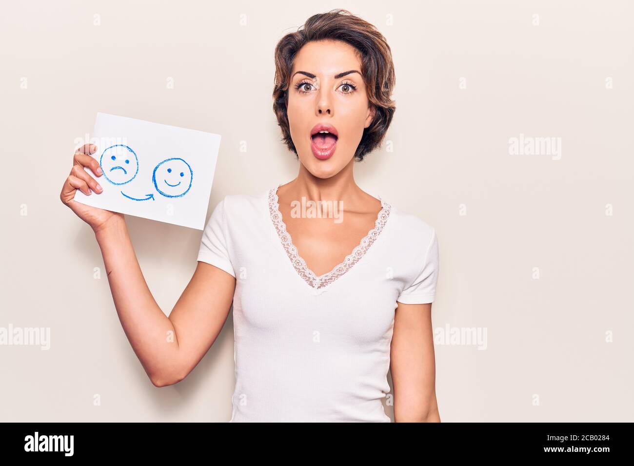 Young beautiful woman holding sad to happy emotion paper scared and ...