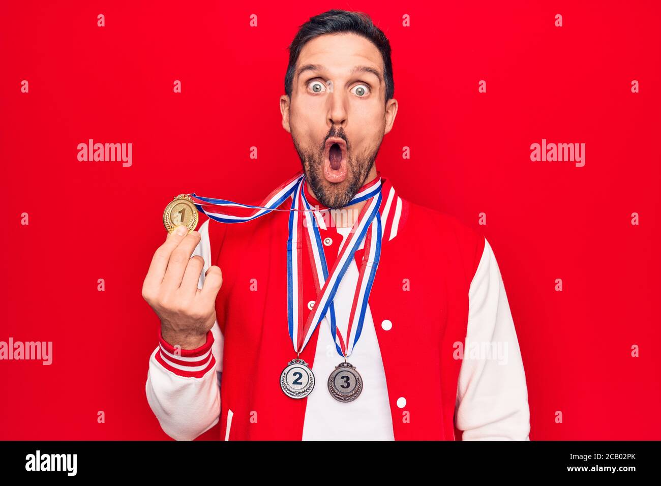 Young handsome sportsman winning medals standing over isolated red ...
