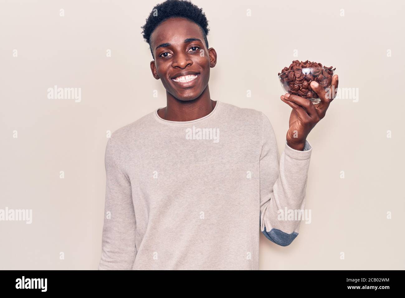 Young african american man holding chocolate cereals looking positive ...