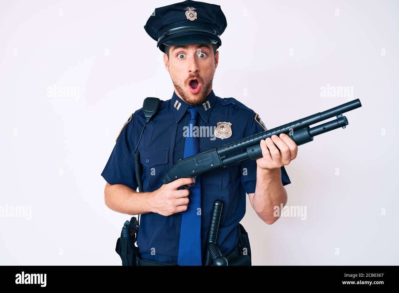 Young caucasian man wearing police uniform holding shotgun afraid and ...