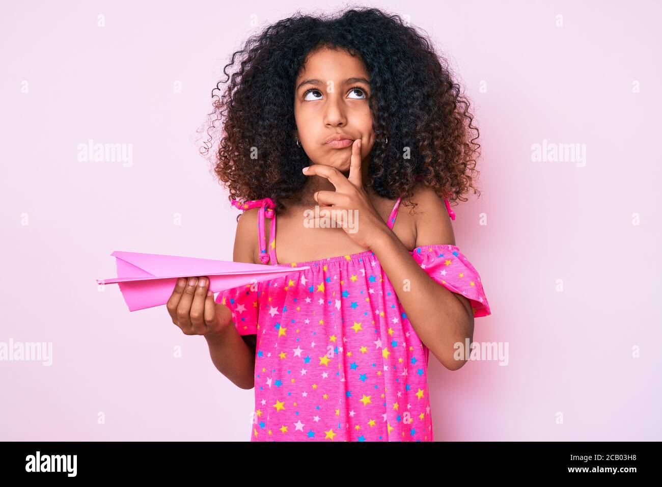 African american child with curly hair holding paper airplane serious ...