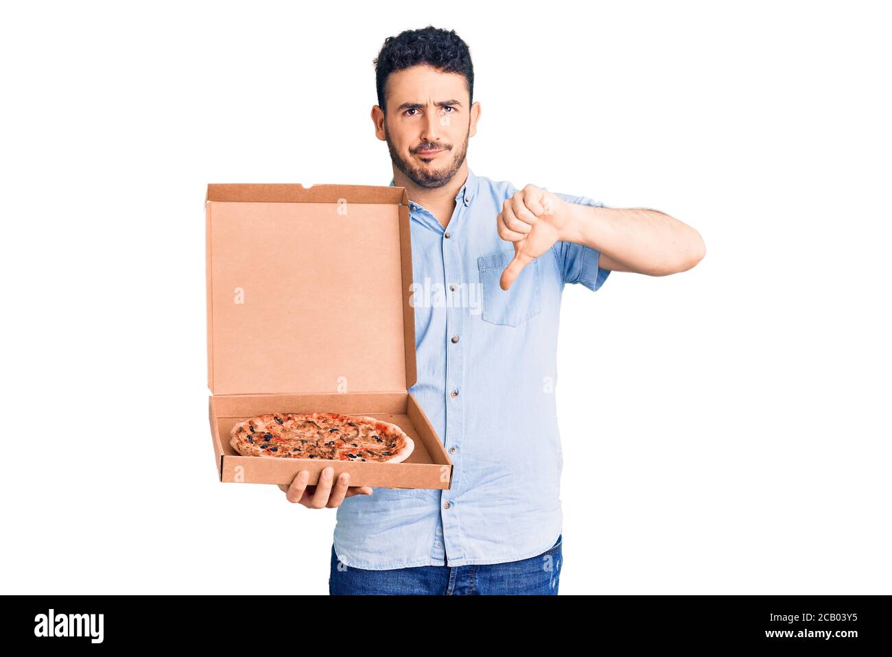 Young hispanic man holding delivery pizza box with angry face, negative ...