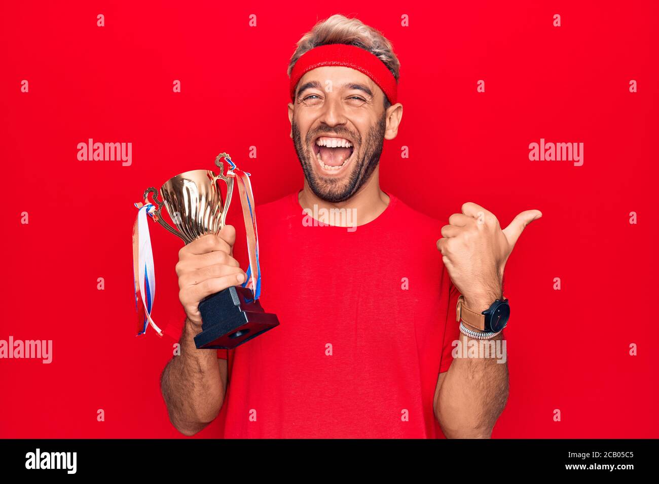 Young handsome blond sportsman with beard winning trophy over isolated ...