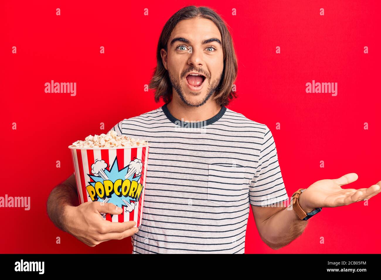 Young handsome man holding popcorn celebrating achievement with happy ...