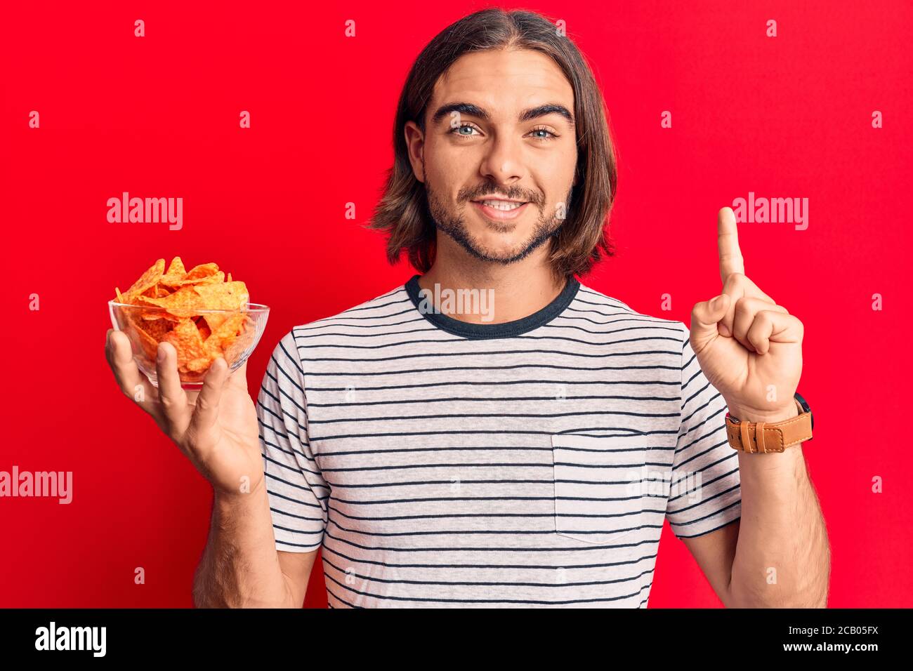 Young handsome man holding nachos potato chips smiling with an idea or ...