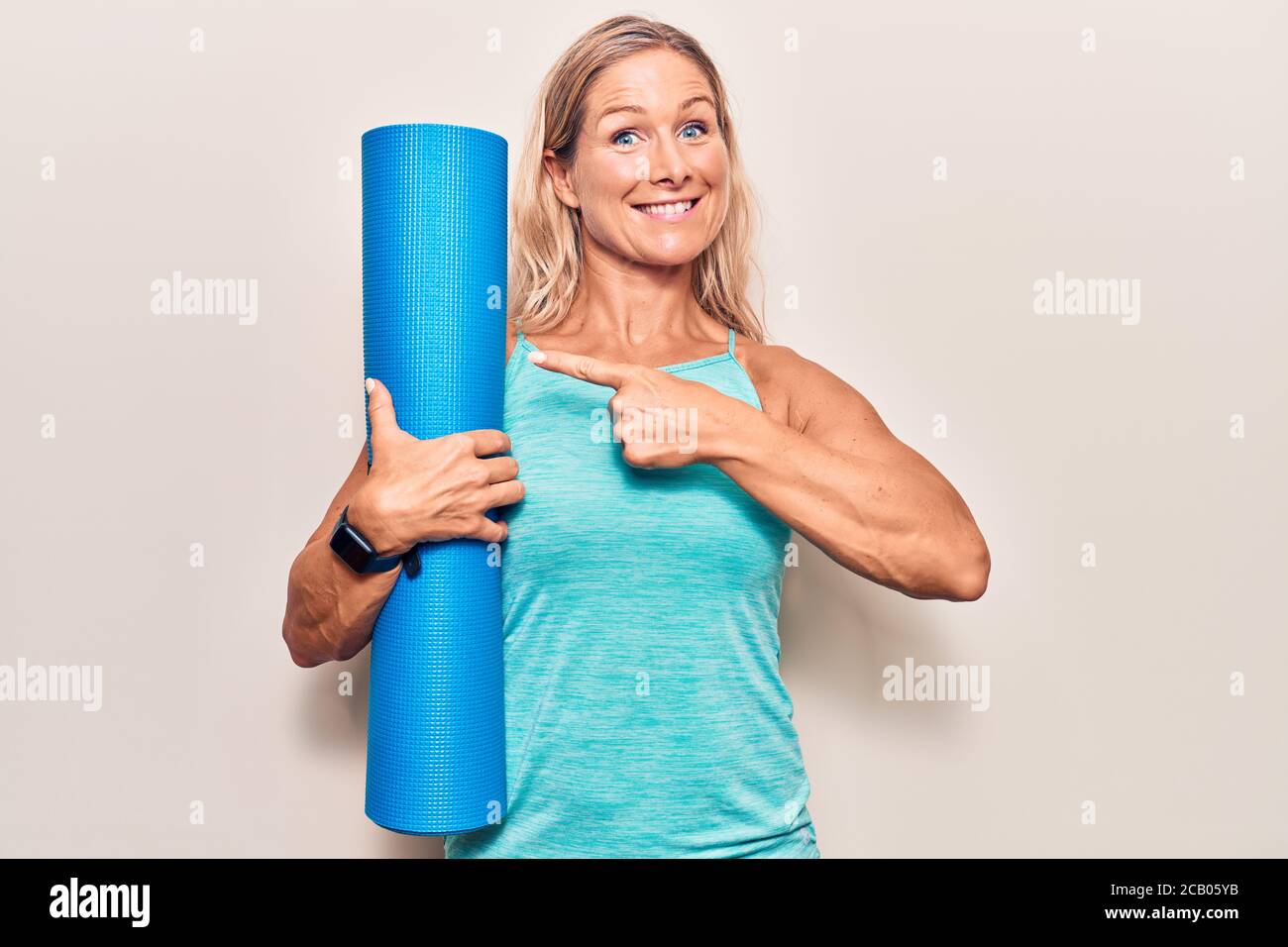 Middle age caucasian blonde woman holding yoga mat smiling happy ...