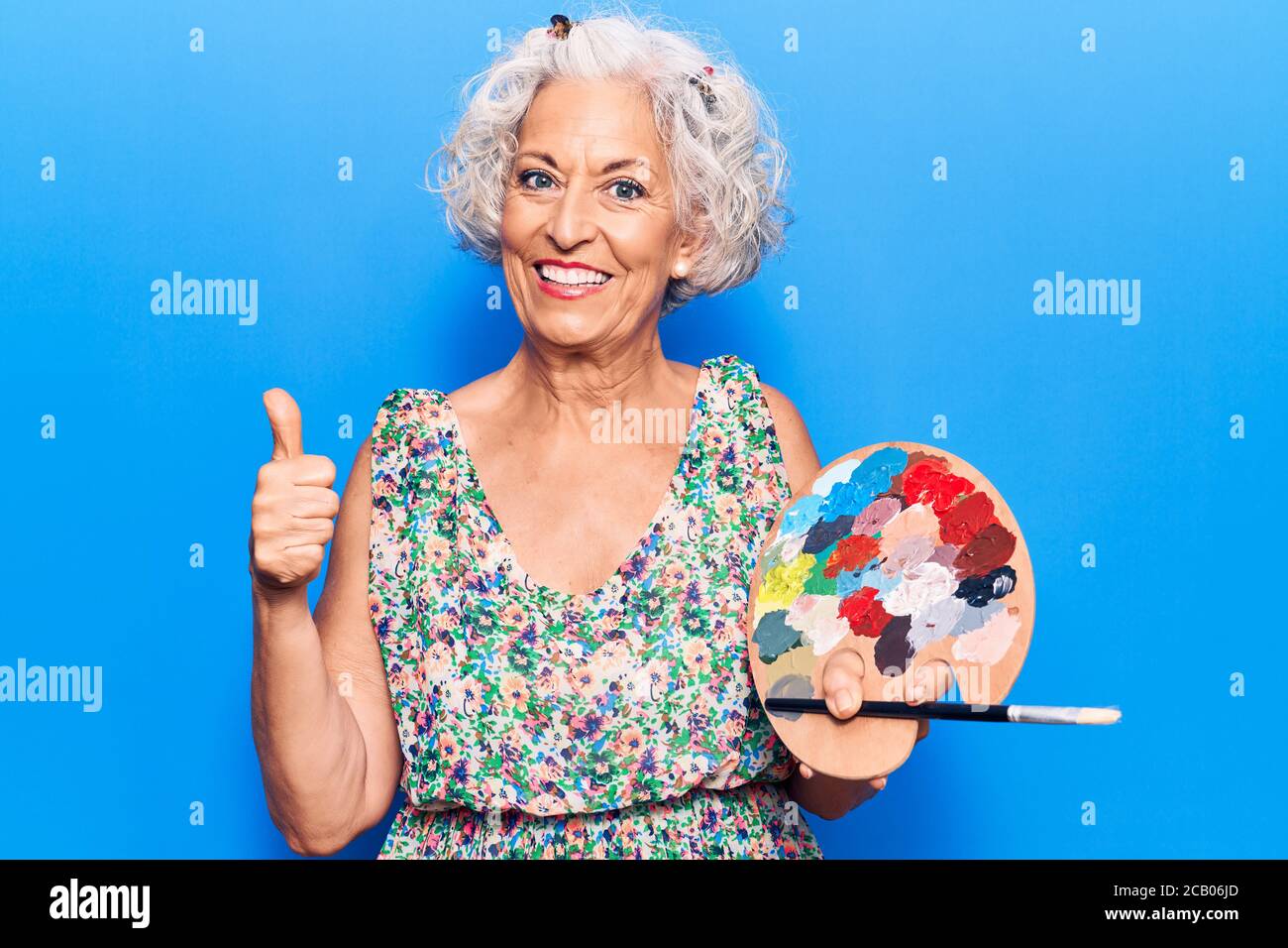 Senior grey-haired woman holding paintbrush and palette smiling happy ...