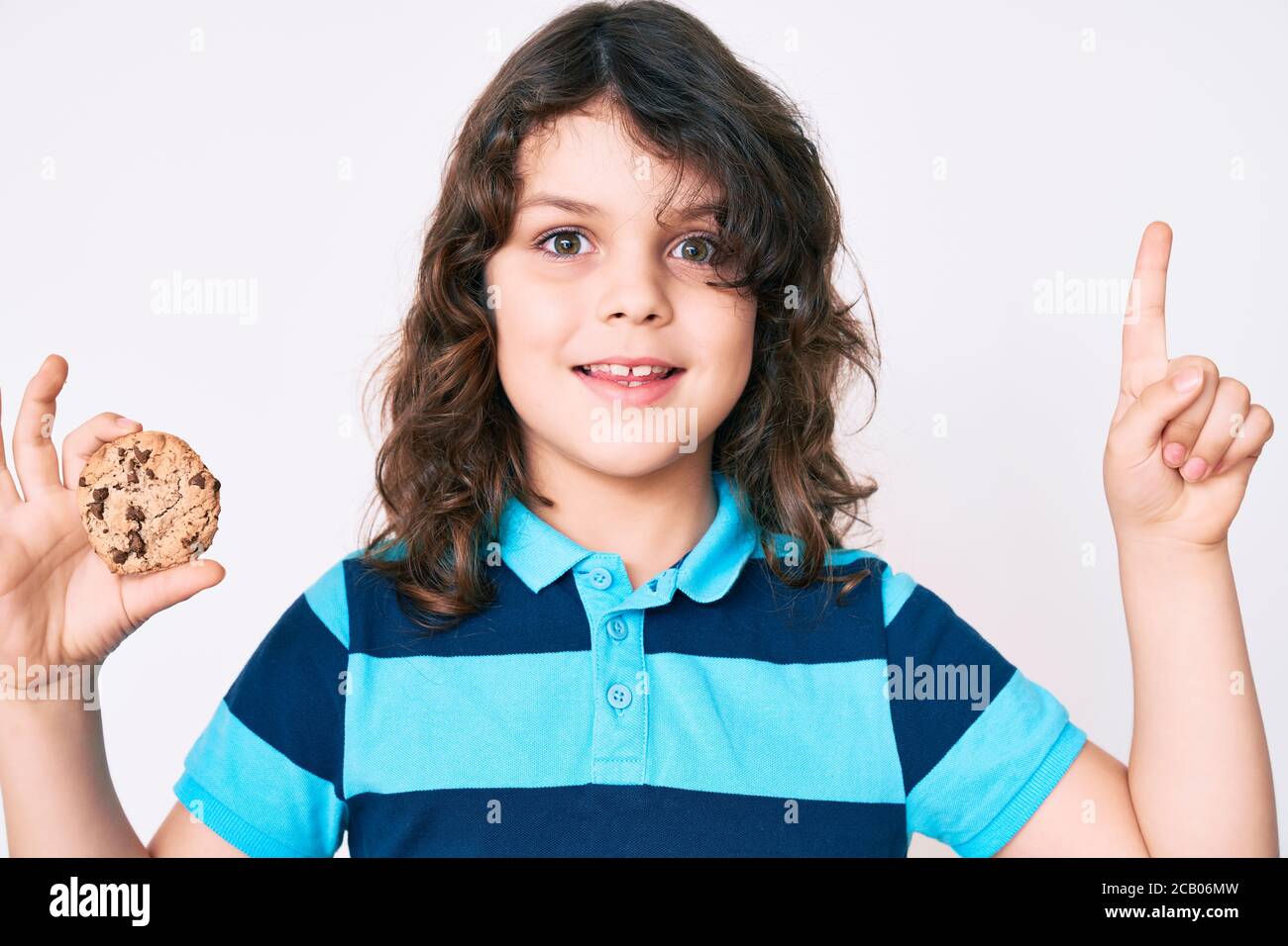 Cute hispanic child with long hair holding cookie smiling with an idea ...