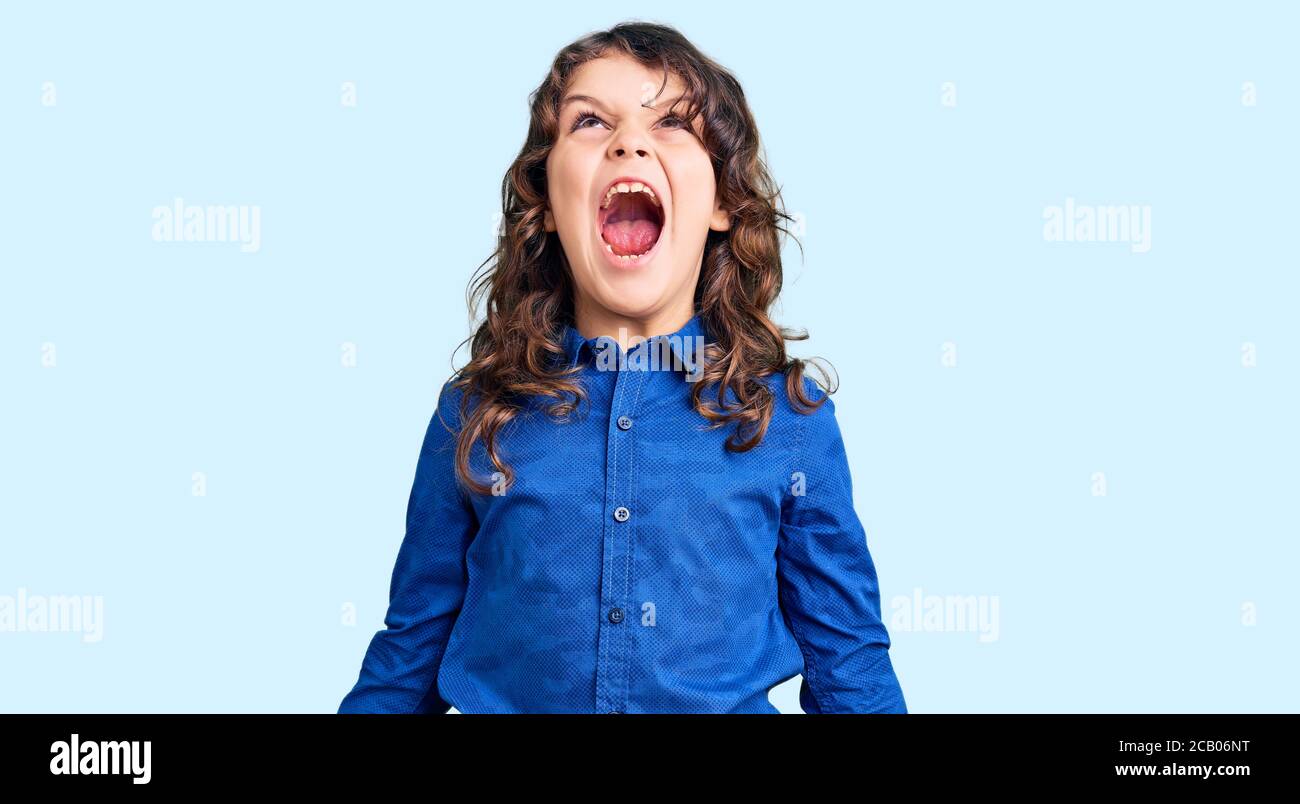Cute child with long hair wearing casual clothes crazy and mad shouting ...